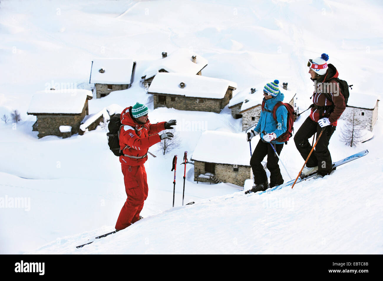 three young skiers on a snow-covered slope over the roofs of the winter ...