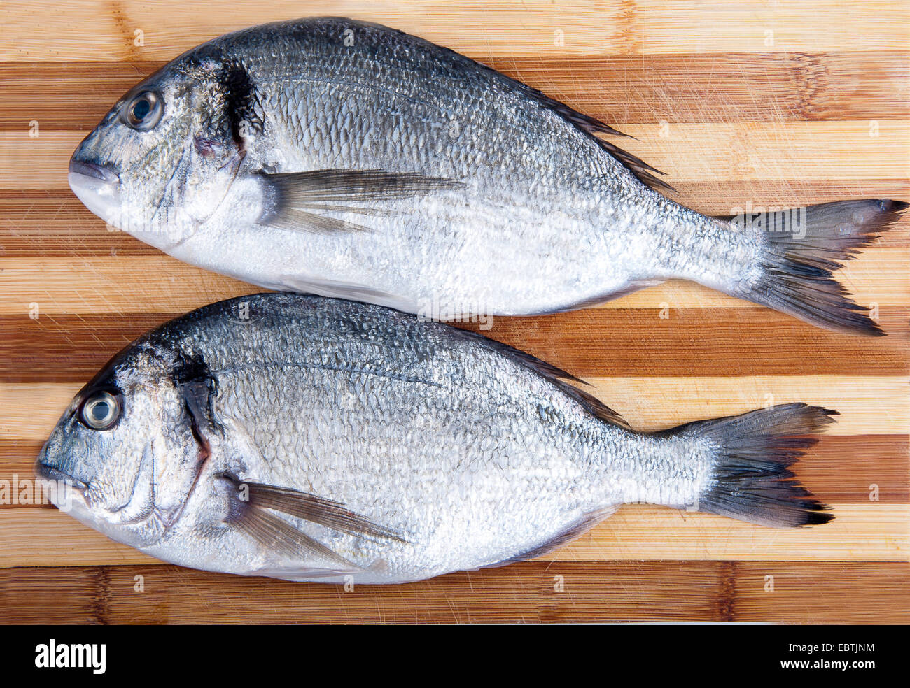 two fresh sea bream on a cutting board Stock Photo - Alamy