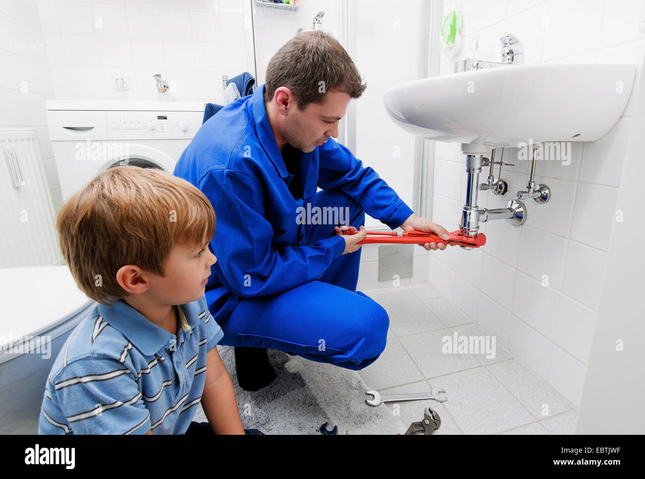 little boy watching a plumber repairing a sink in bathroom Stock Photo ...