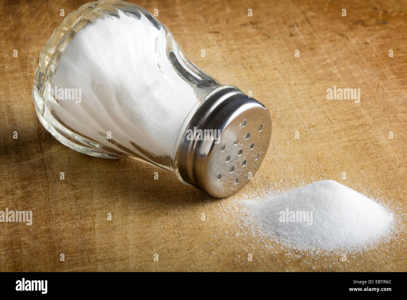 Traditional glass salt cellar and spilled salt on a wood background ...