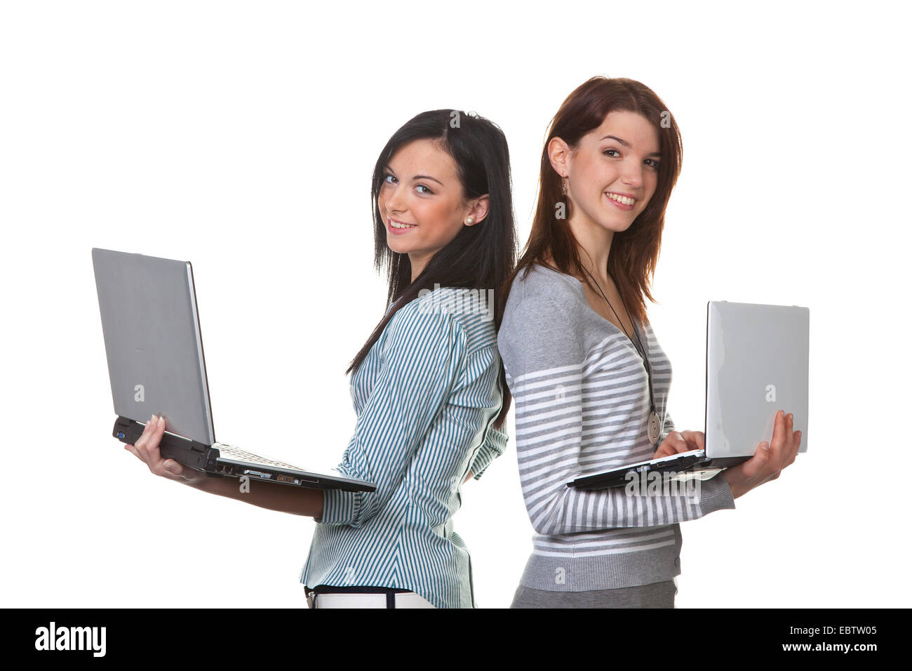 two young women standing back to back smiling with their opened laptops ...