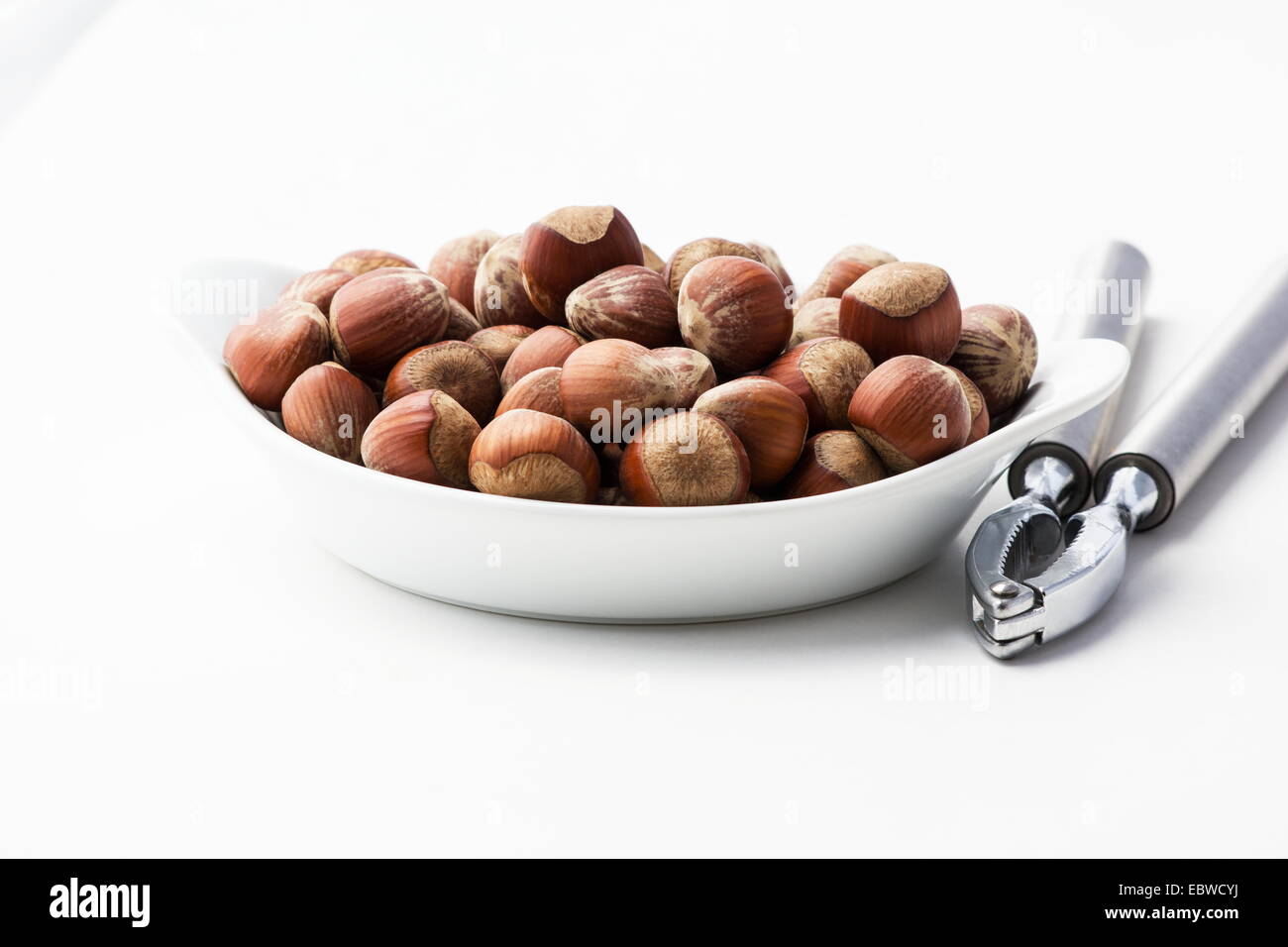 Hazelnuts in a white bowl and a nutcracker on white background Stock ...