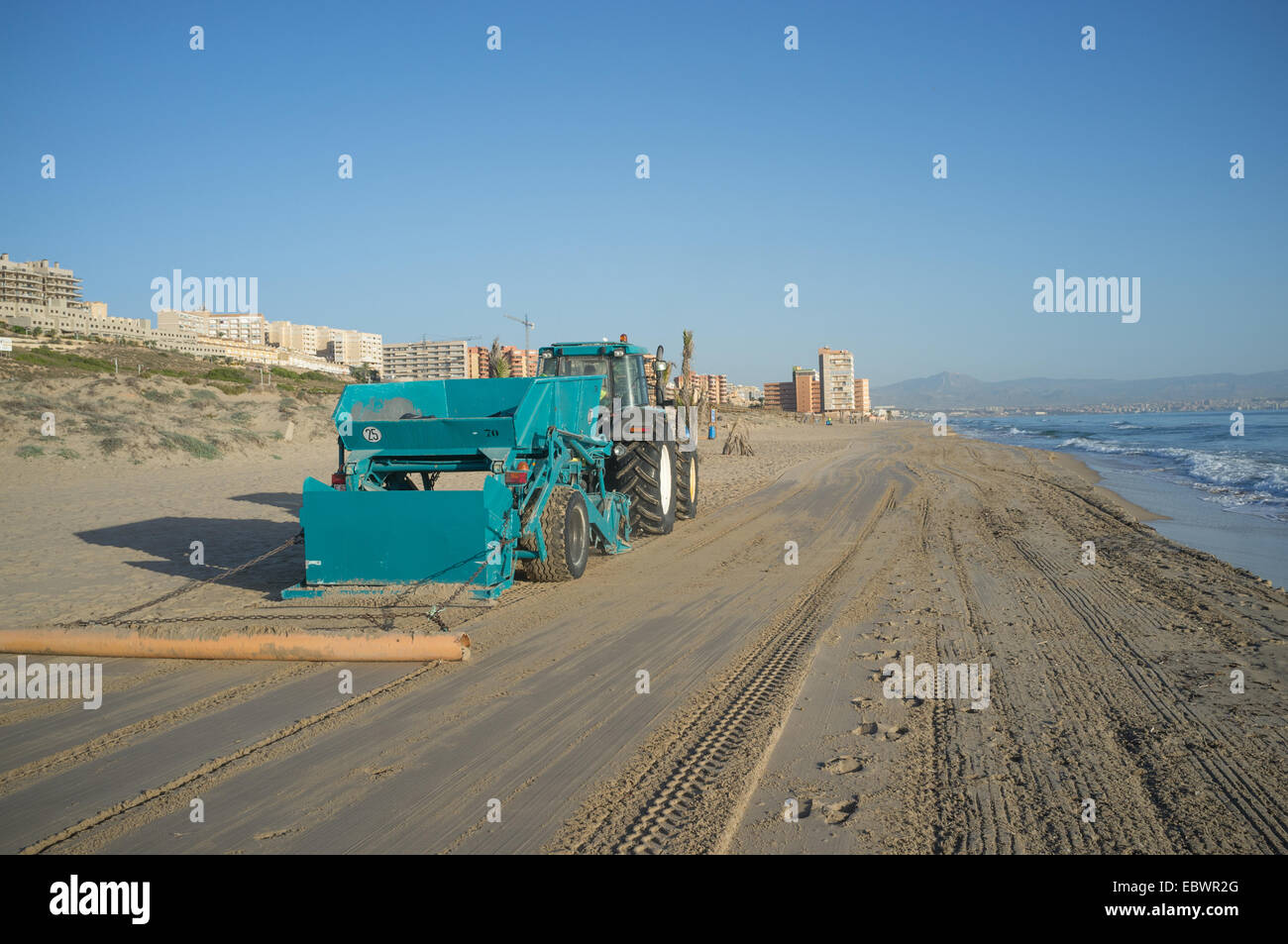 A tractor with a trailer cleaning a beach in the early hours of the ...