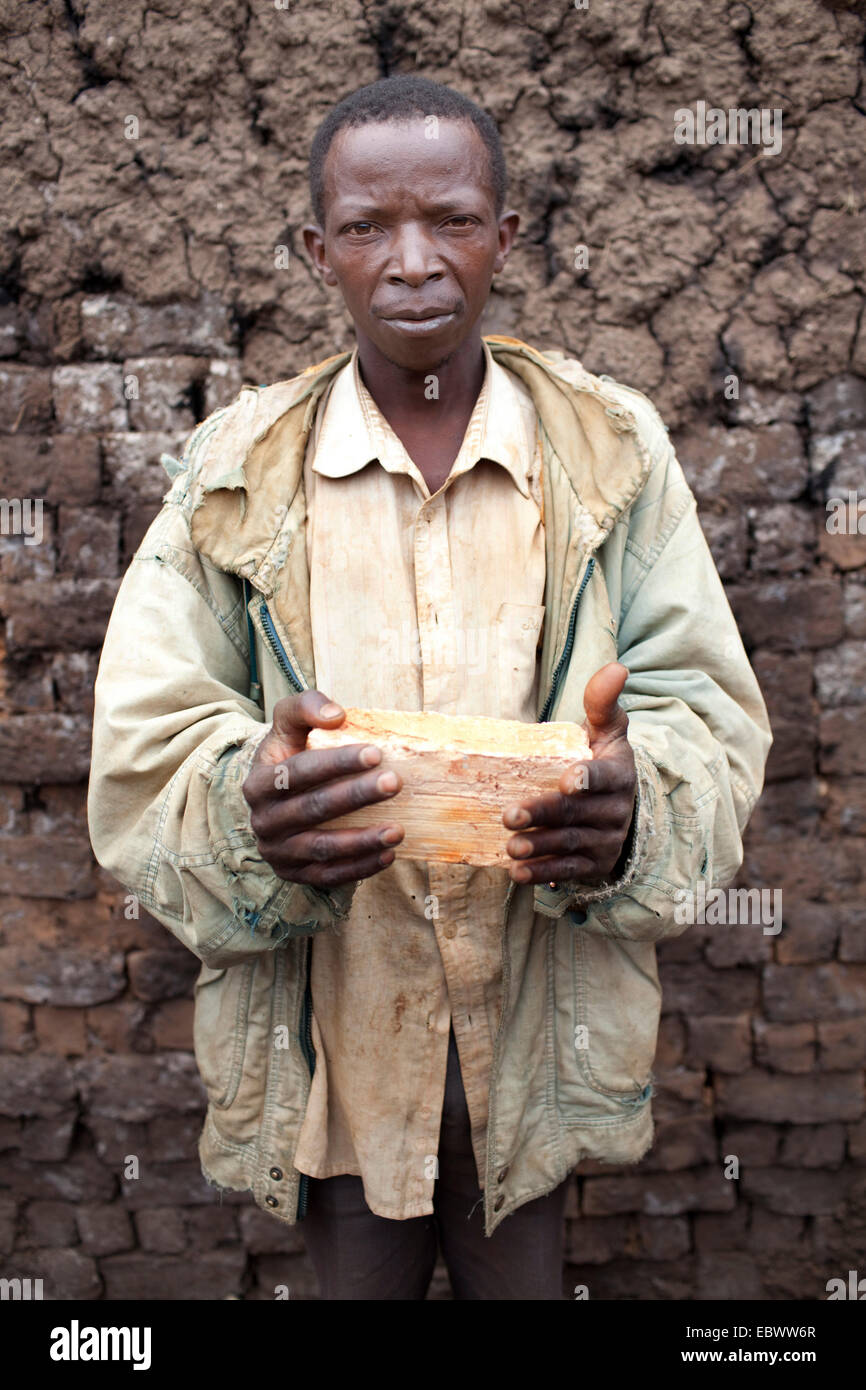man holding a log of wood and standing in front of mud wall, Burundi ...
