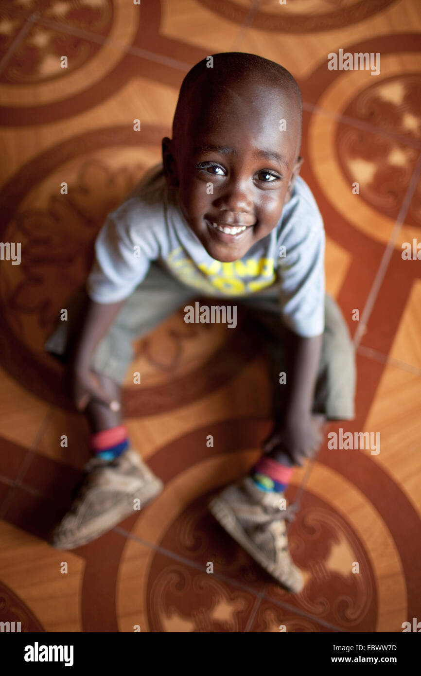 little boy sitting on a tiled floor looking up at the camera over his ...