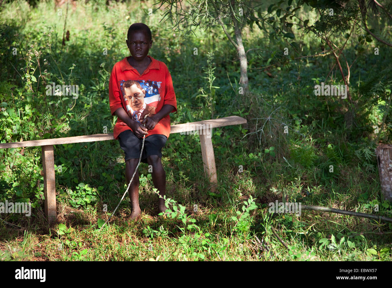 boy sitting on wooden bench, US president Obama is printed on his t ...