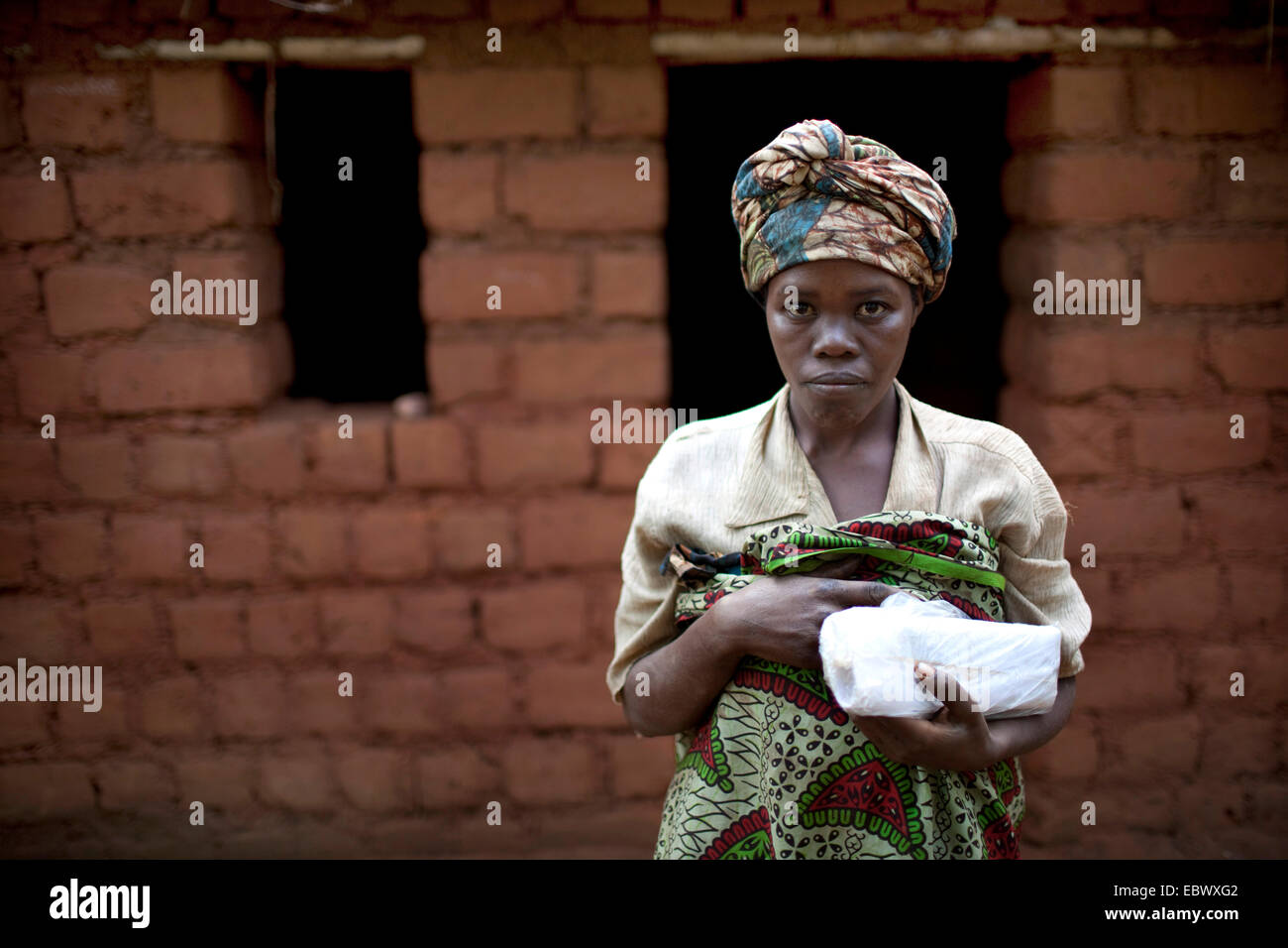 woman in traditional clothes standing in front of a mud brick house ...