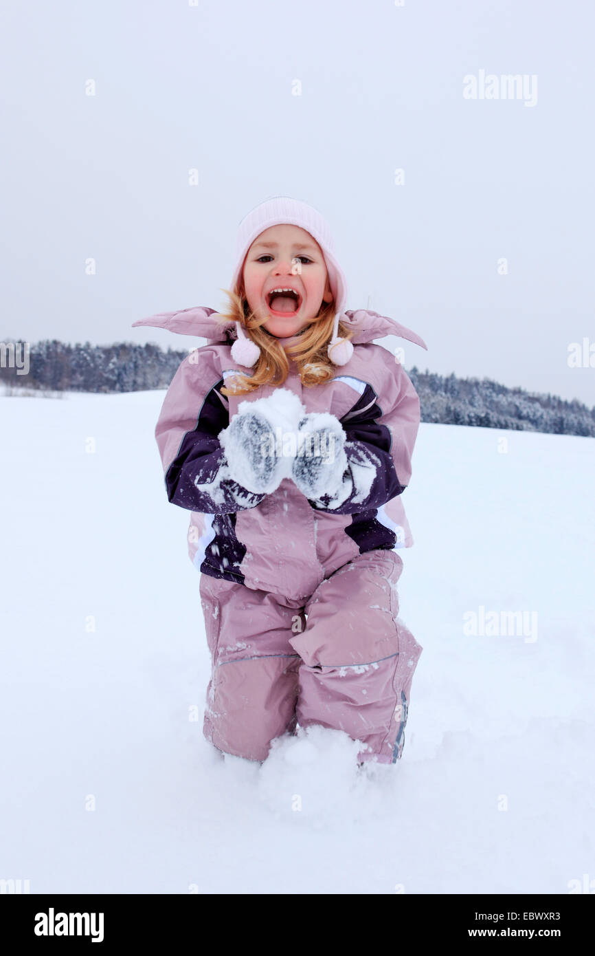 little girl laughing while kneeing in the snow forming a snowball ...