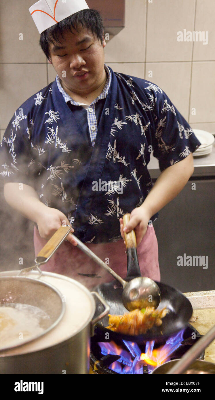 cook in the kitchen of a Mongolian restaurant preparing a meal in a wok ...