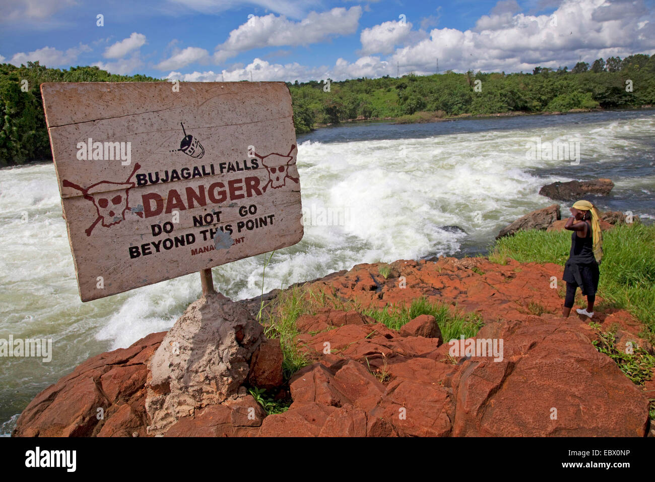 Female tourist standing at the Bujagali waterfalls, danger sign hinting ...