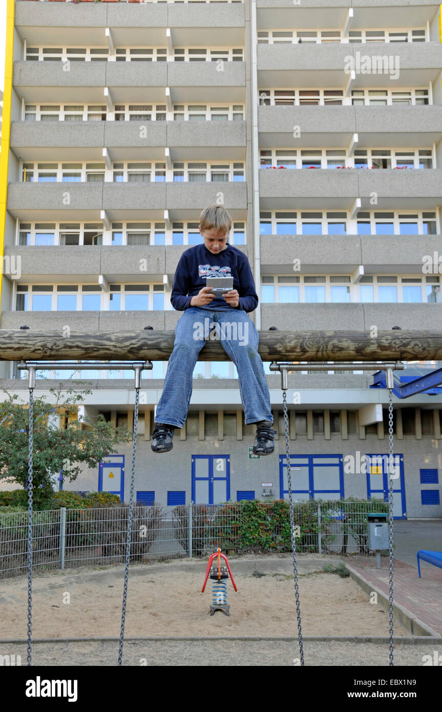 boy playing with gameboy in front of tower block, Germany, Chorweiler ...