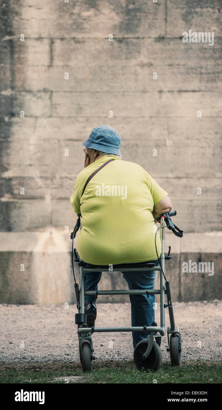 Senior woman sitting on walker in front of stone wall Stock Photo - Alamy