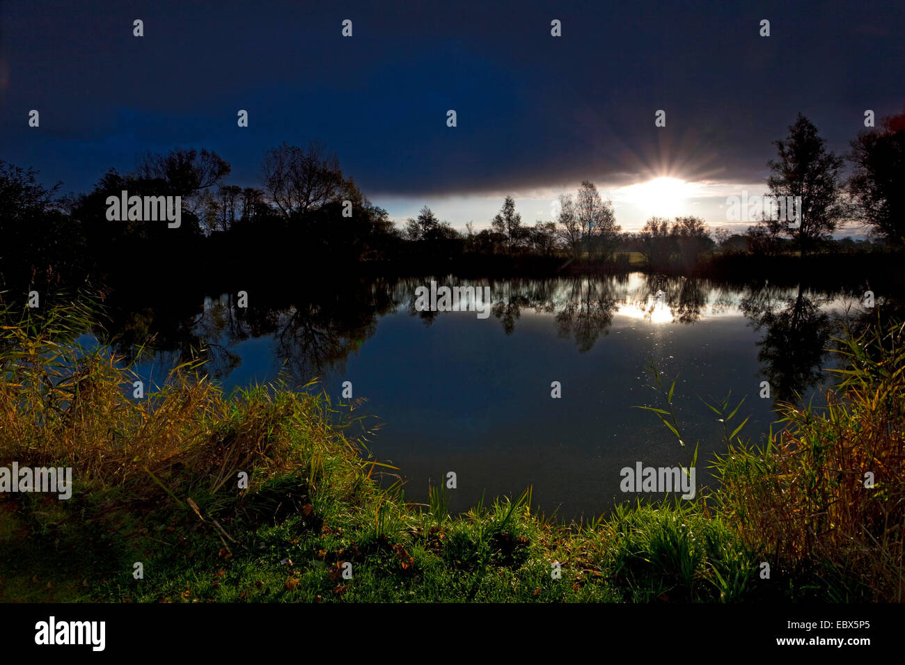 setting sun shining on a lake through a hole in a cloud cover, Germany ...