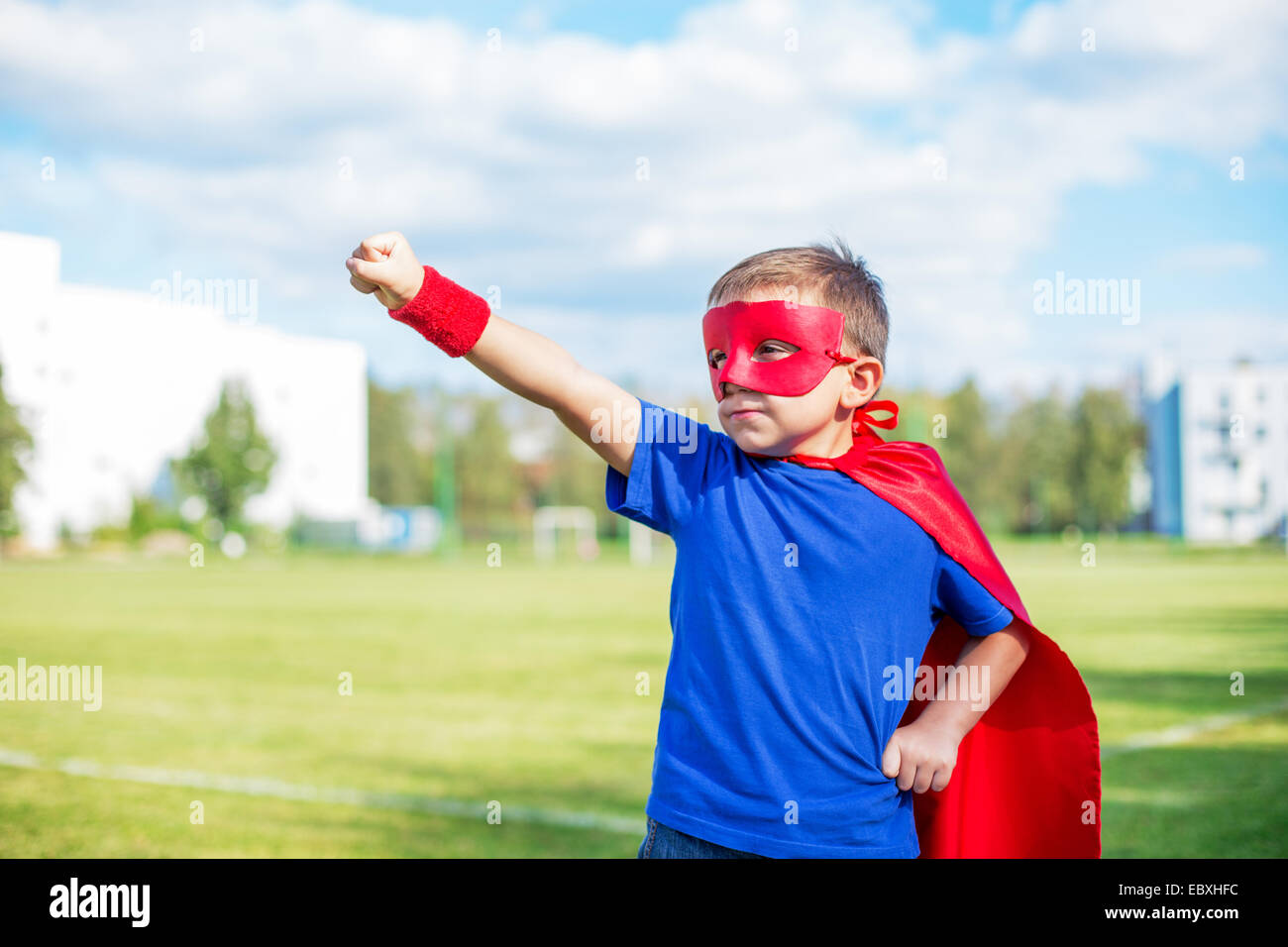 Boy dressed in cape and mask standing with his arm raised and calling ...