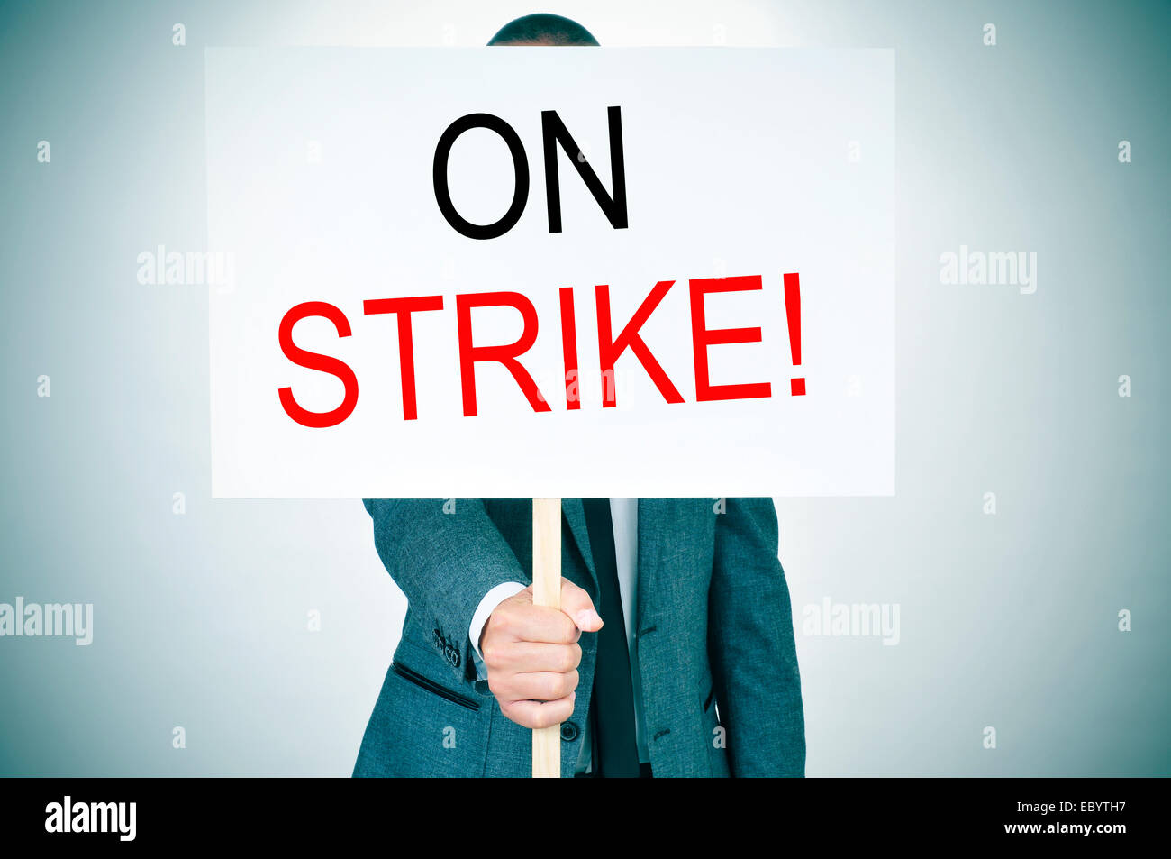 a young man in suit with a protest signboard with the text on strike ...