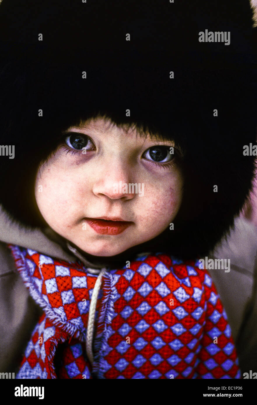 Tiny child in huge fur hat plays in the snow at recess in Kindergarten ...