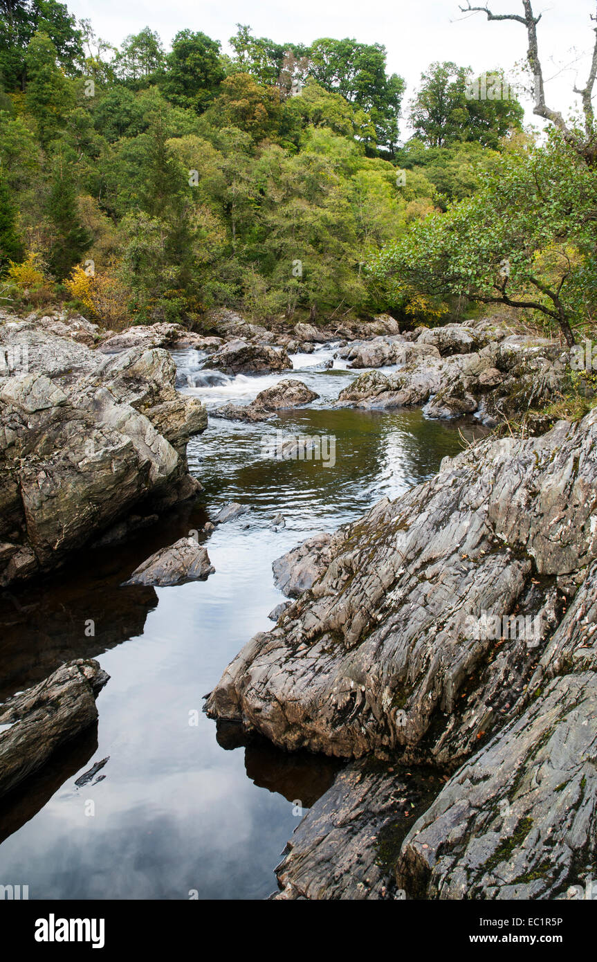 Portrait image of a small river in Scotland flanked by large rocks and ...