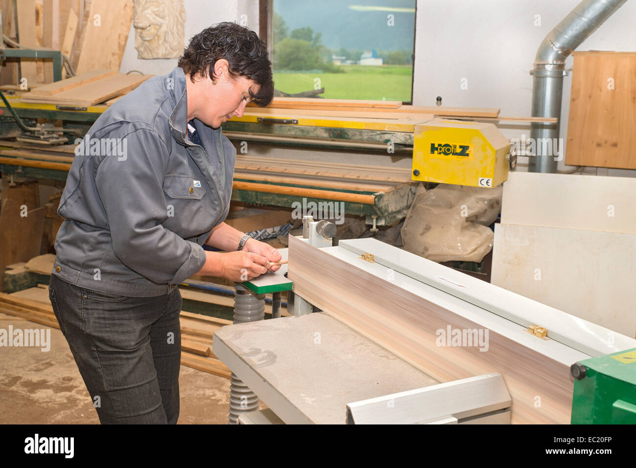 Young farmer repairing a hay rake, sharpening teeth on the belt sander ...