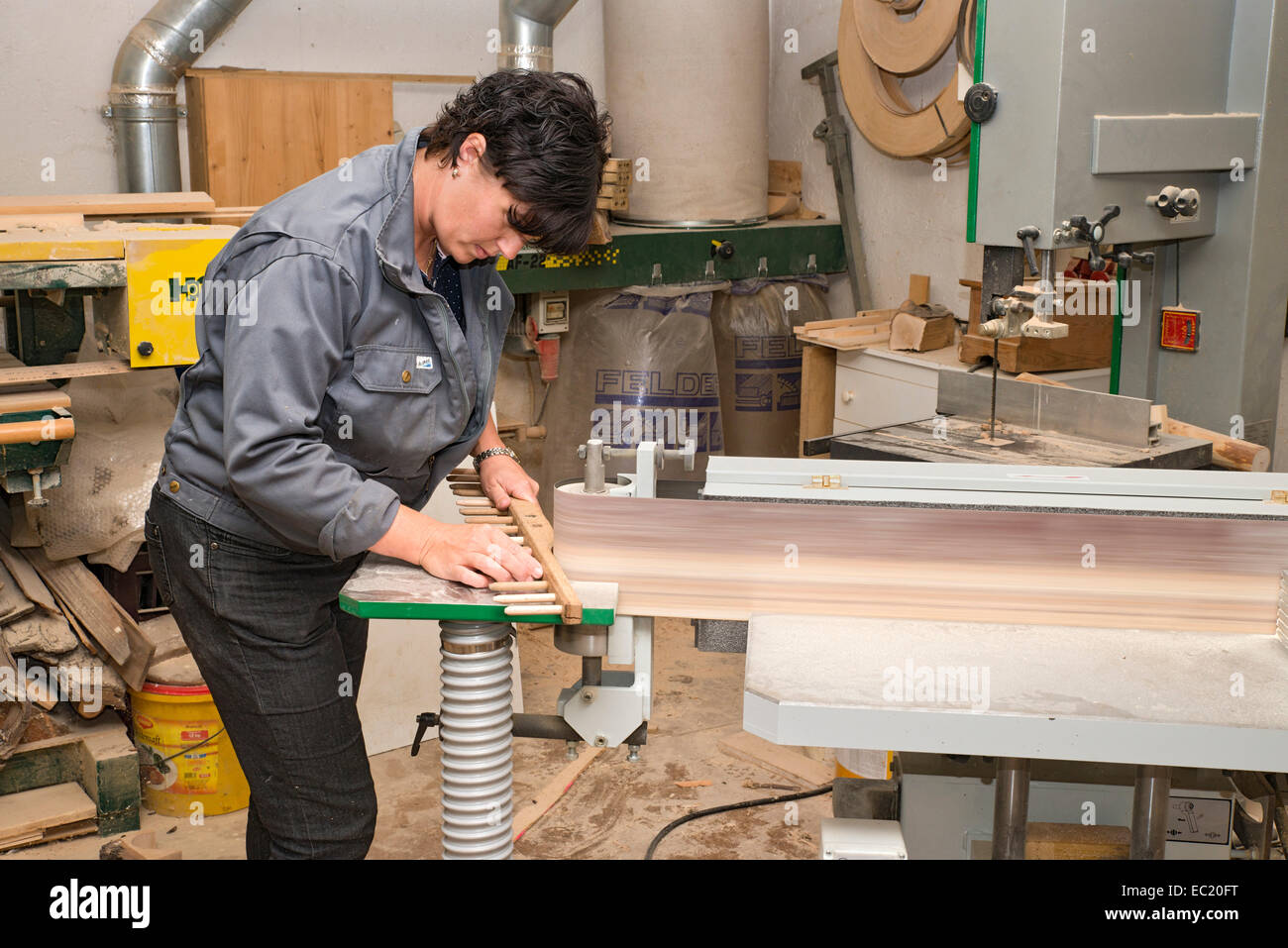 Young farmer repairing a hay rake, sharpening teeth on the belt sander ...