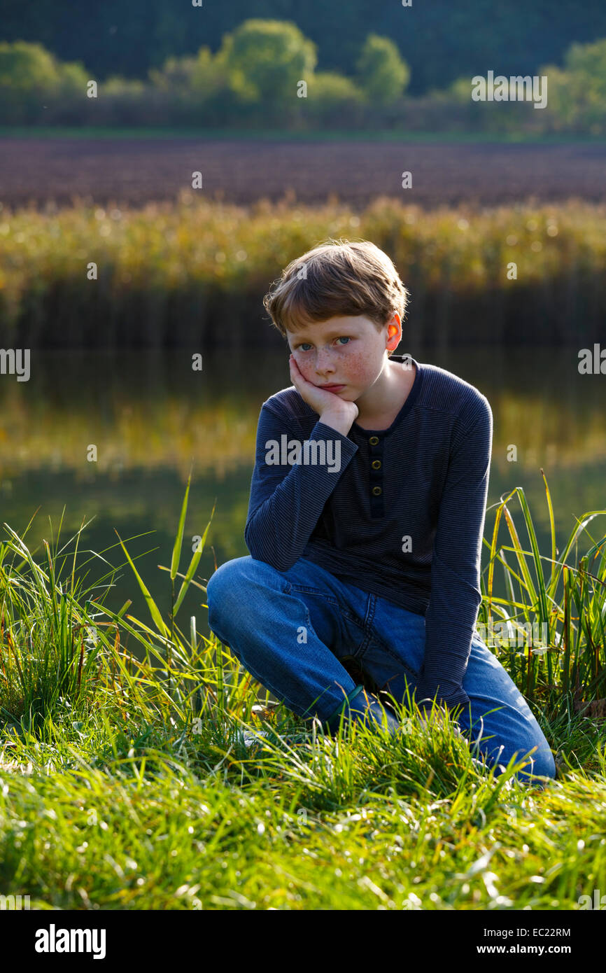 Sad boy sitting on a small lake, Wandersleben, Thuringia, Germany Stock ...