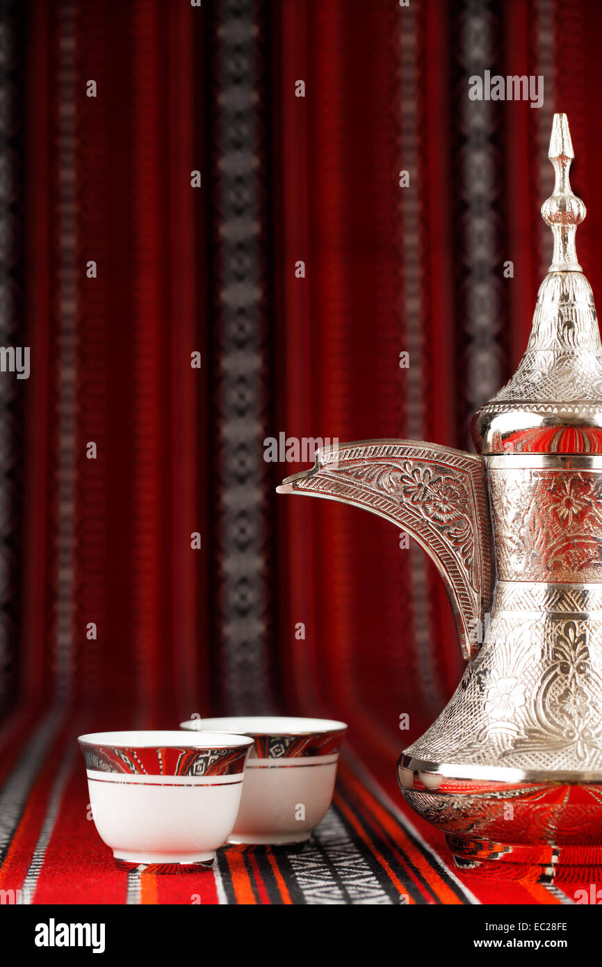 Ornate Arabian tea cups and a dallah are placed on traditional red ...