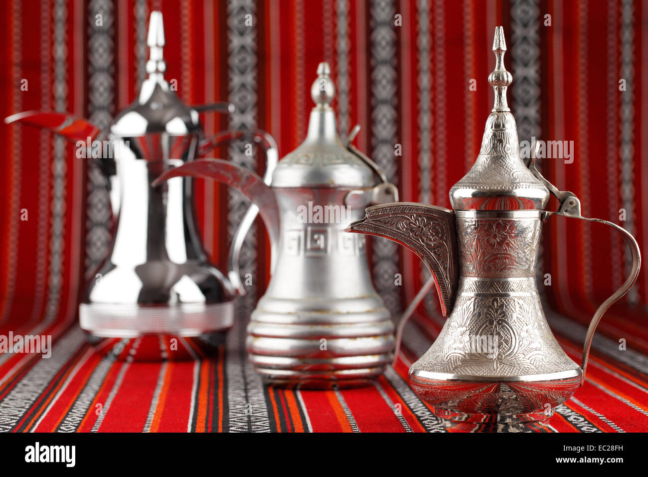 Three ornate Dallah are placed on traditional red fabric from the ...