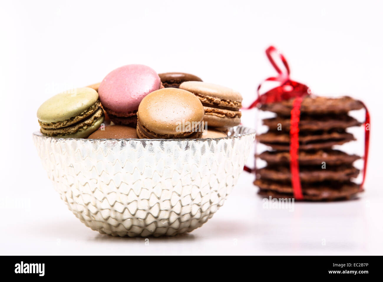 Colored macarons in bowl and chocolate cookies with red ribbon on white ...