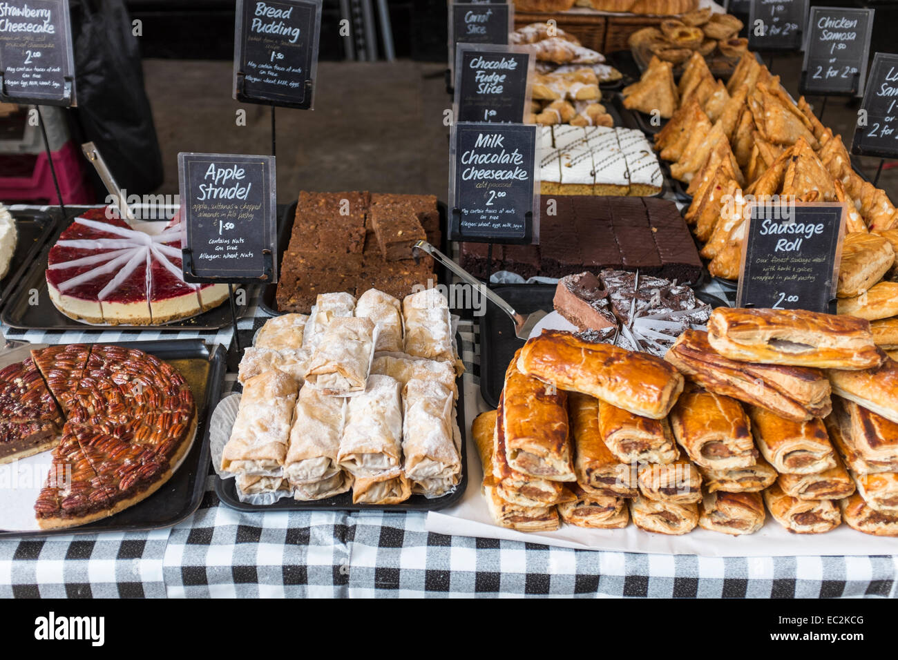 Cakes, pastries and sausage rolls on display for sale on a market stall ...