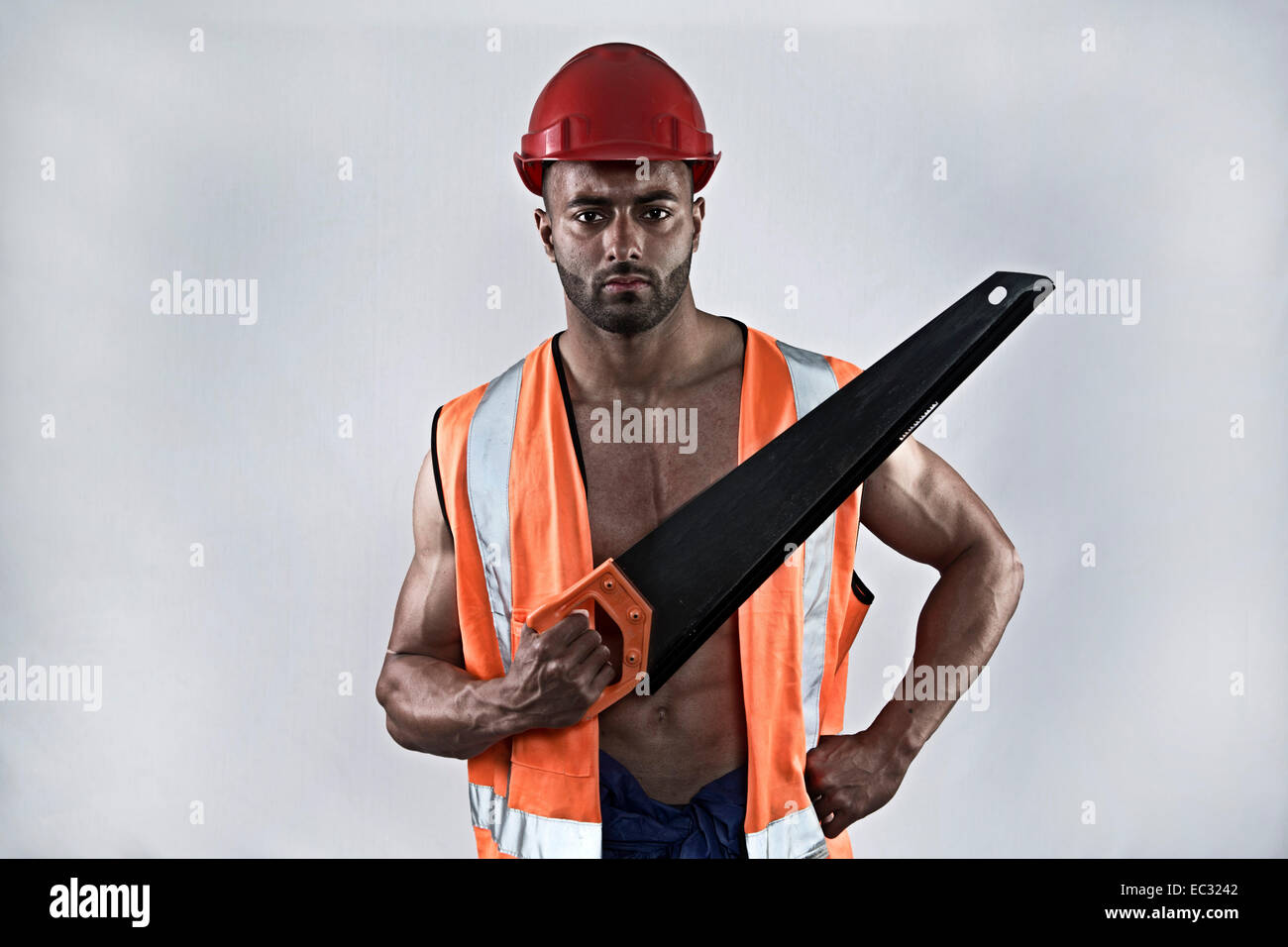 Young fit male shirtless workman with a saw wearing a reflective jacket ...