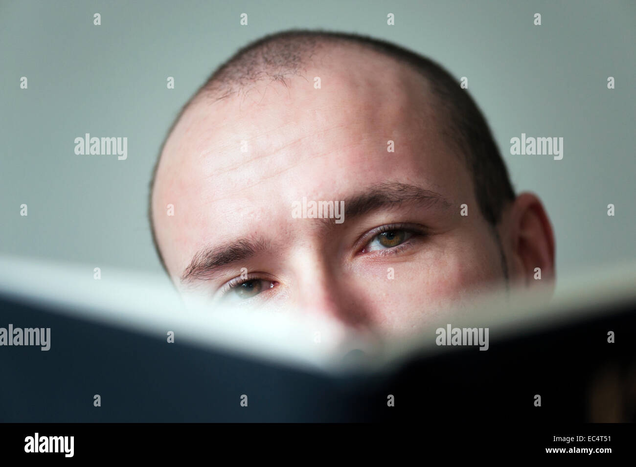 young man looks over the edge of a book on the viewer Stock Photo - Alamy