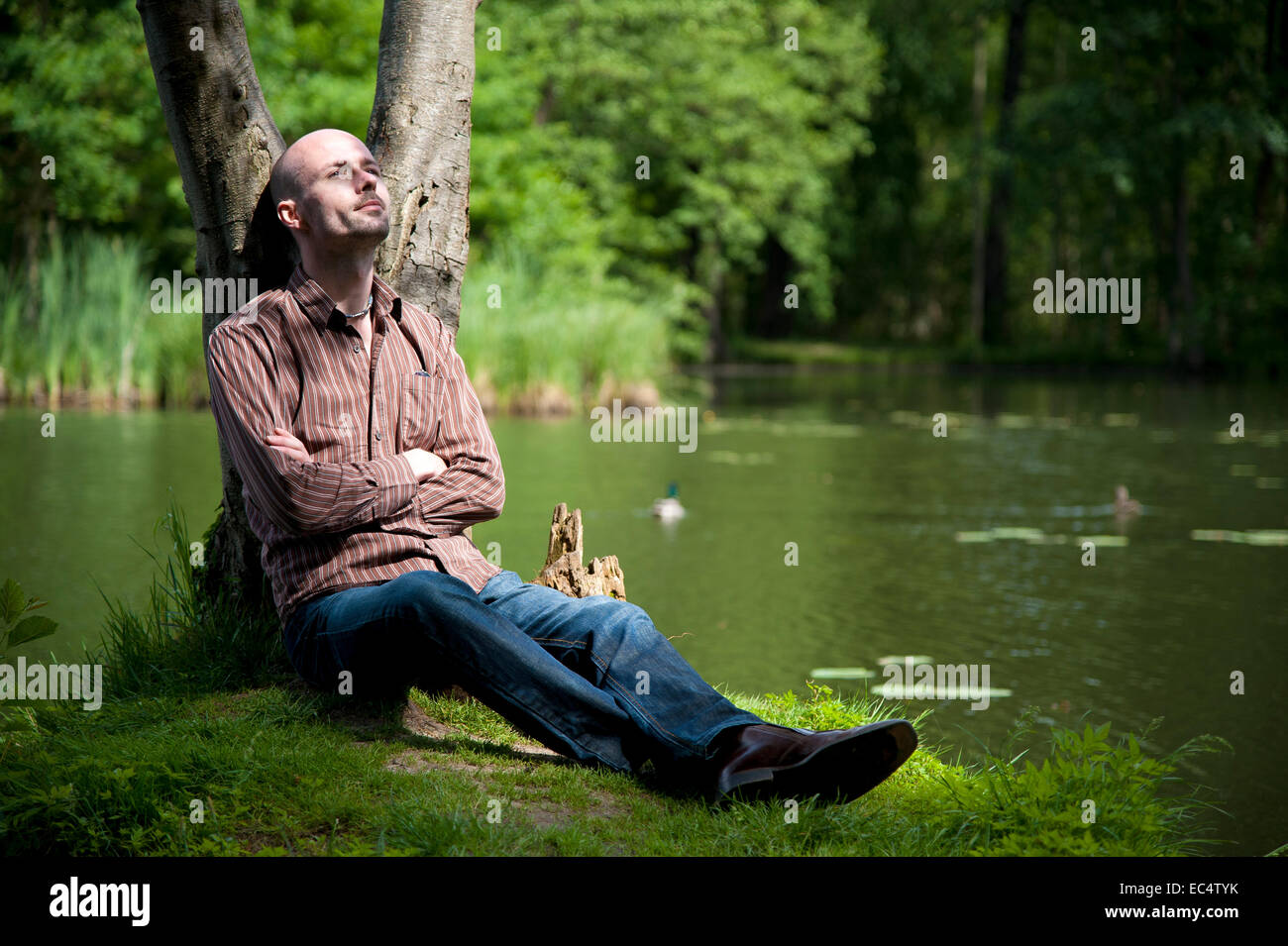 Young man leaning against a tree Stock Photo - Alamy