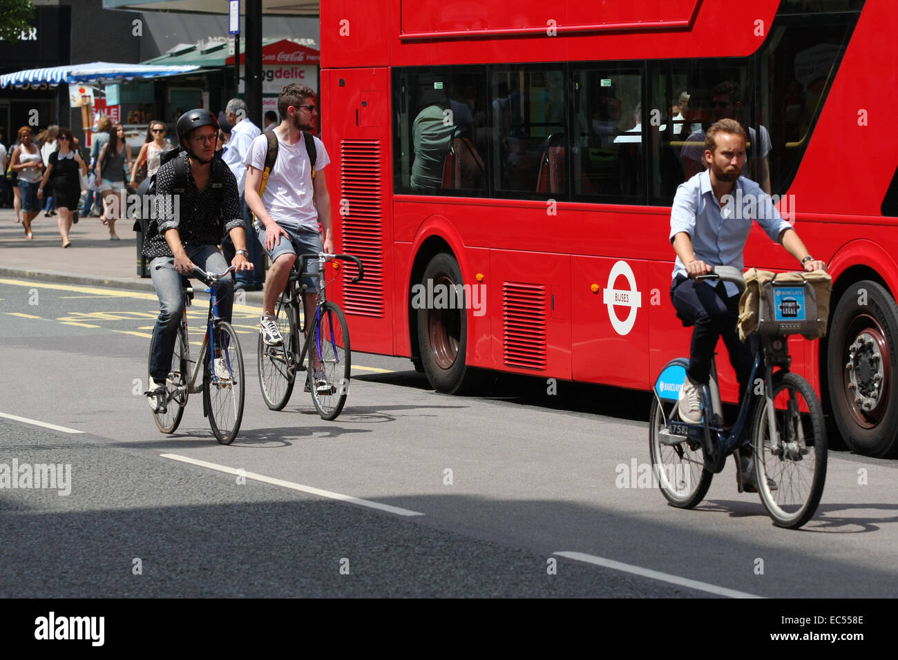 Three cyclists overtaking a red London bus at a bus stop in Oxford ...