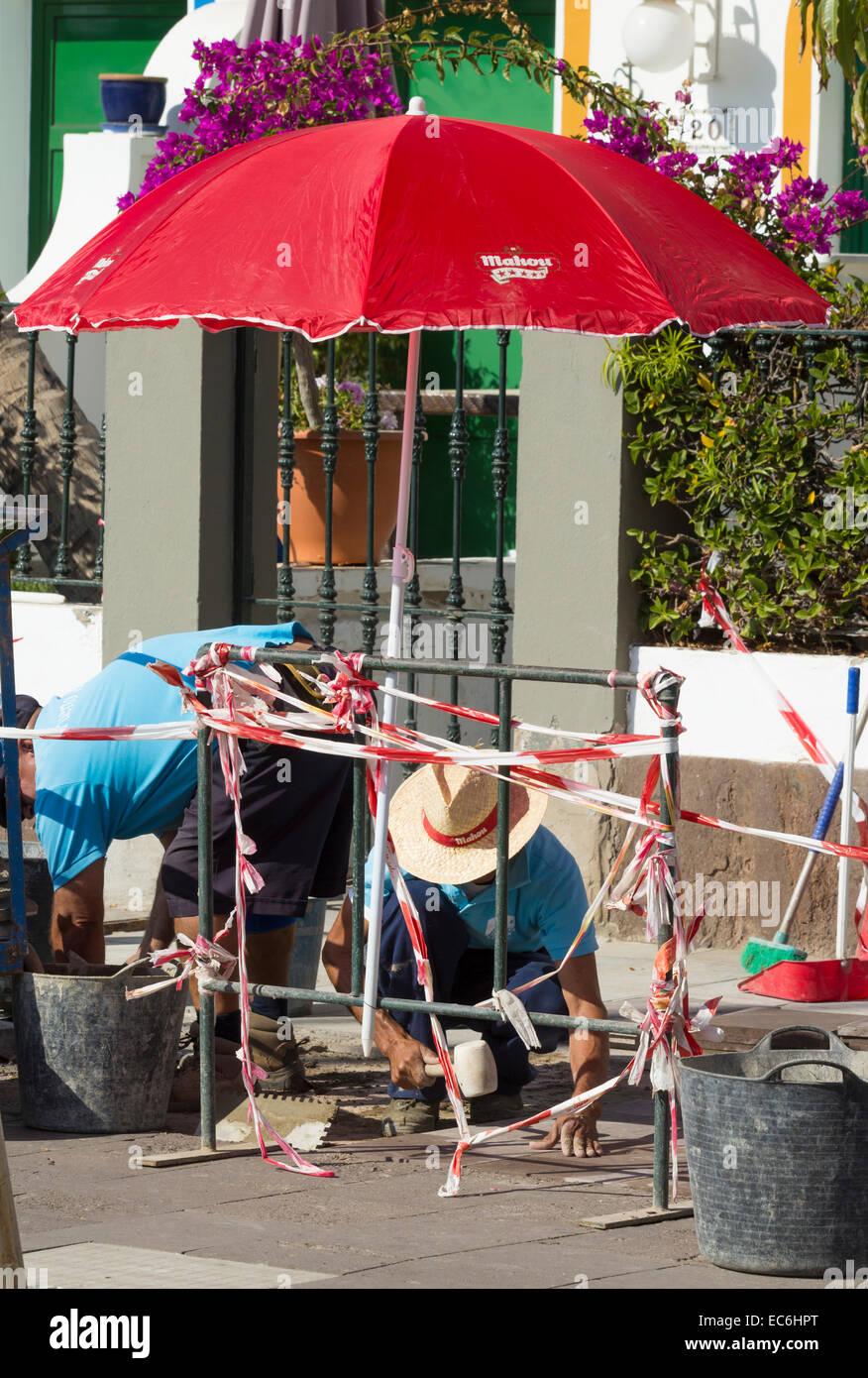 Spanish workmen laying paving stones use beach umbrella to protect them ...