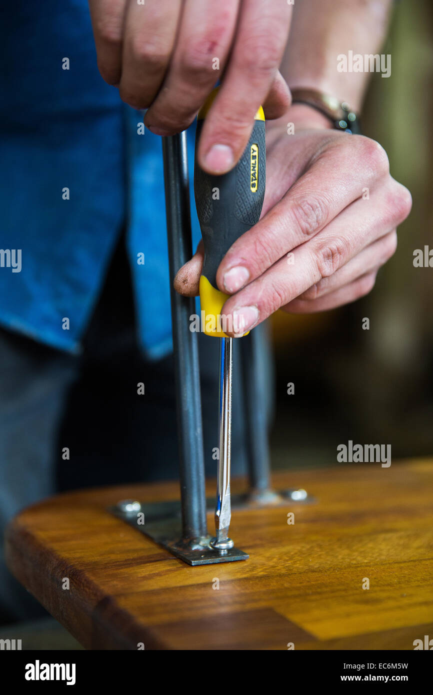 A carpenter screws in some metal legs into a bespoke wooden desk ...
