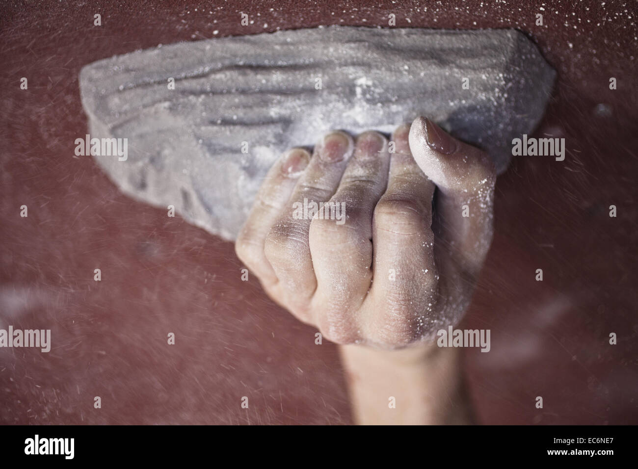 Climbers hand on a grip in a climbing hall, with chalk dust and red ...