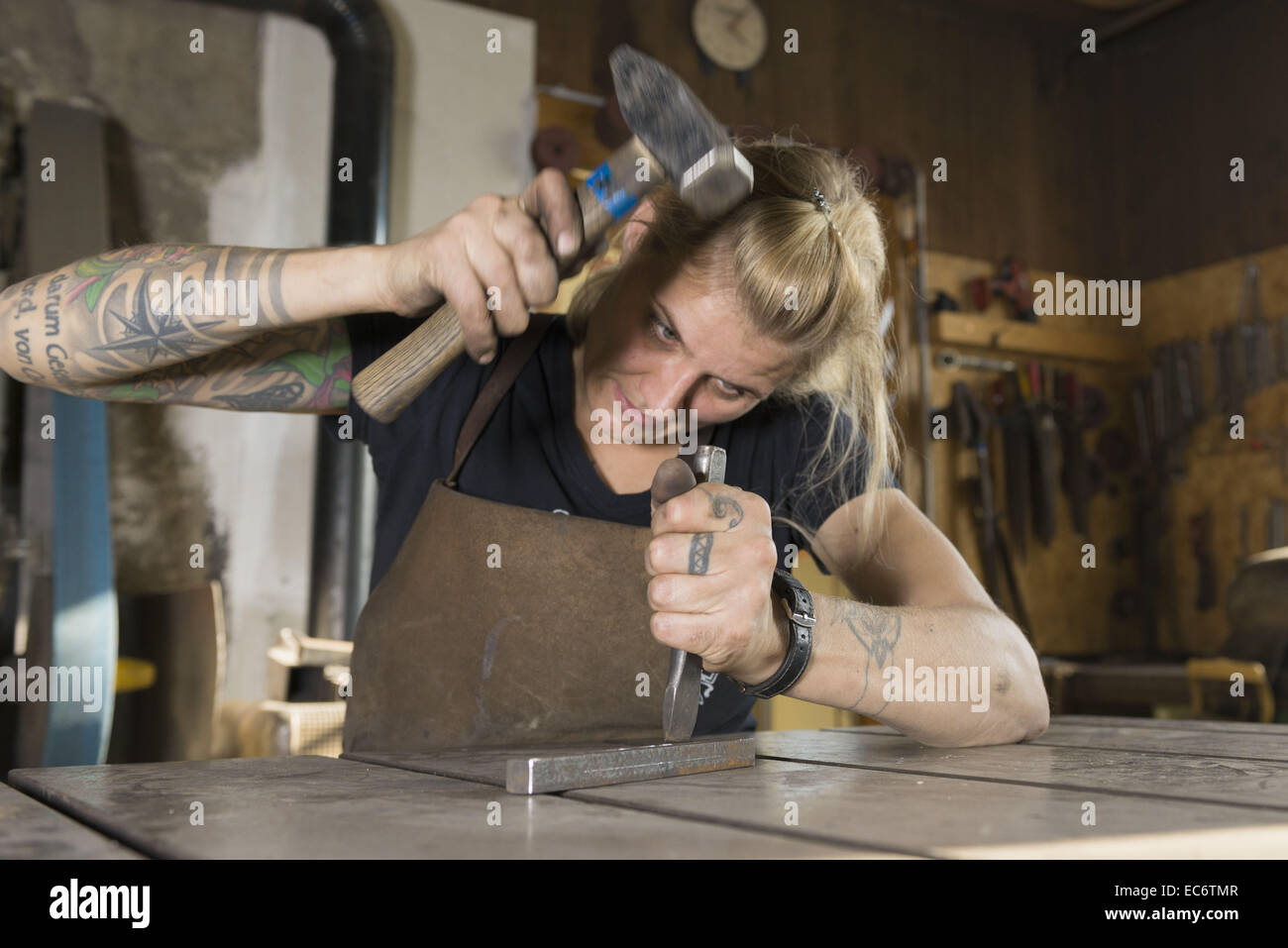young female blacksmith working on a piece of steel with sledge and ...