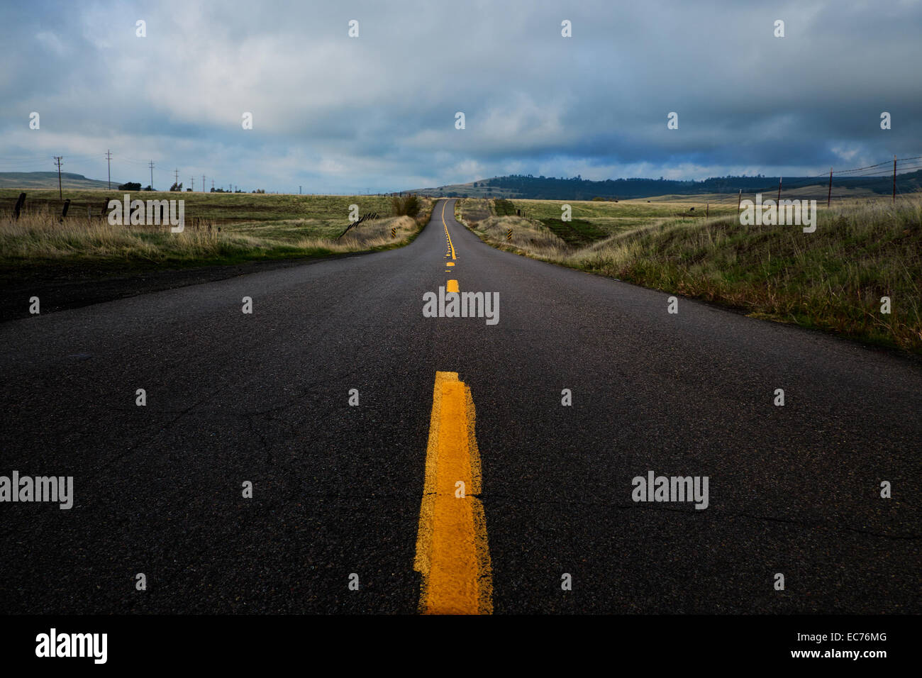 A rural country road passing through ranch land with storm clouds ...