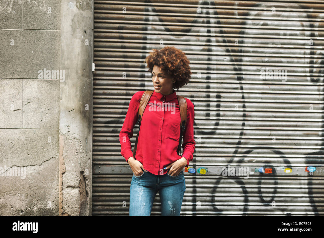 Smiling young woman standing in front of roller shutter with graffiti ...