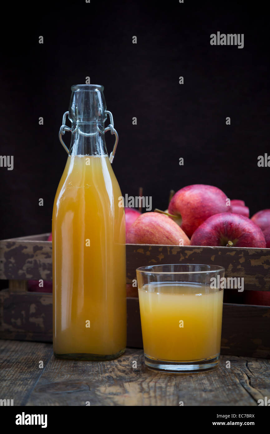 Bottle and glass of apple juice and box with red apples in front of ...