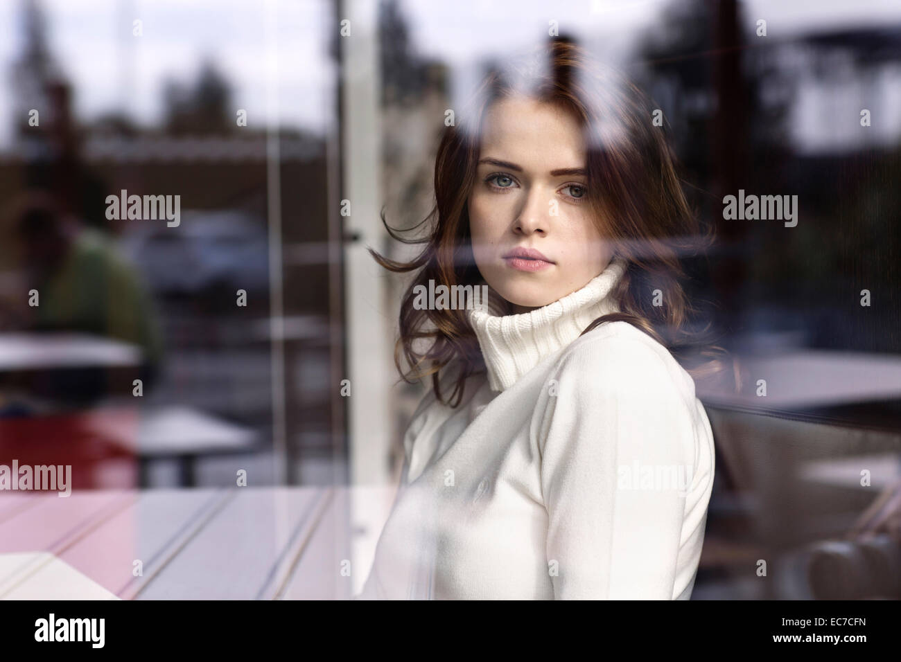 Portrait of young woman looking through window pane of a cafe Stock ...