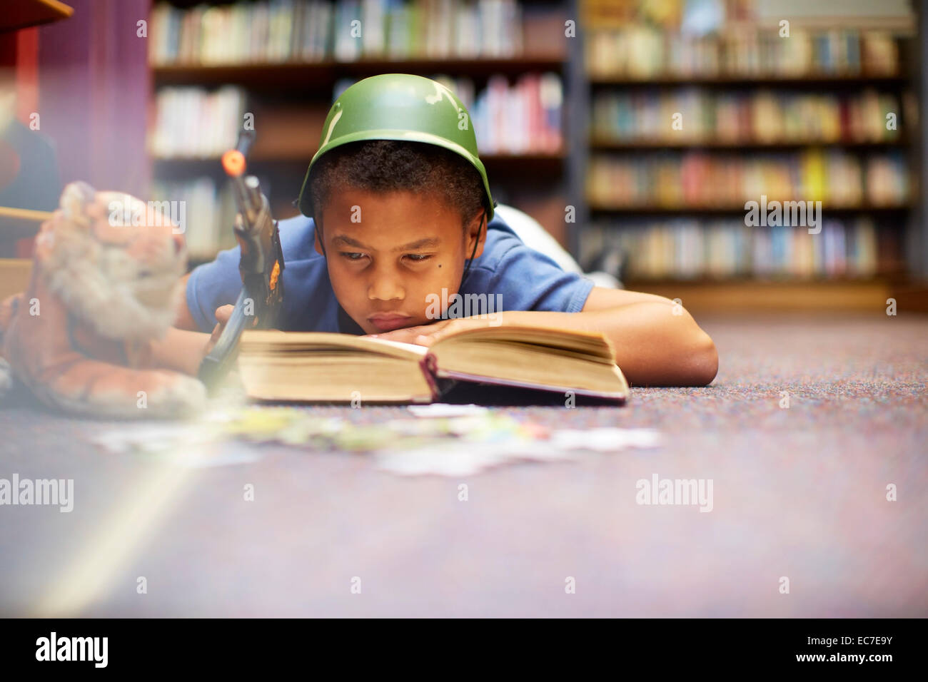 Boy with helmet and gun reading book in library Stock Photo - Alamy