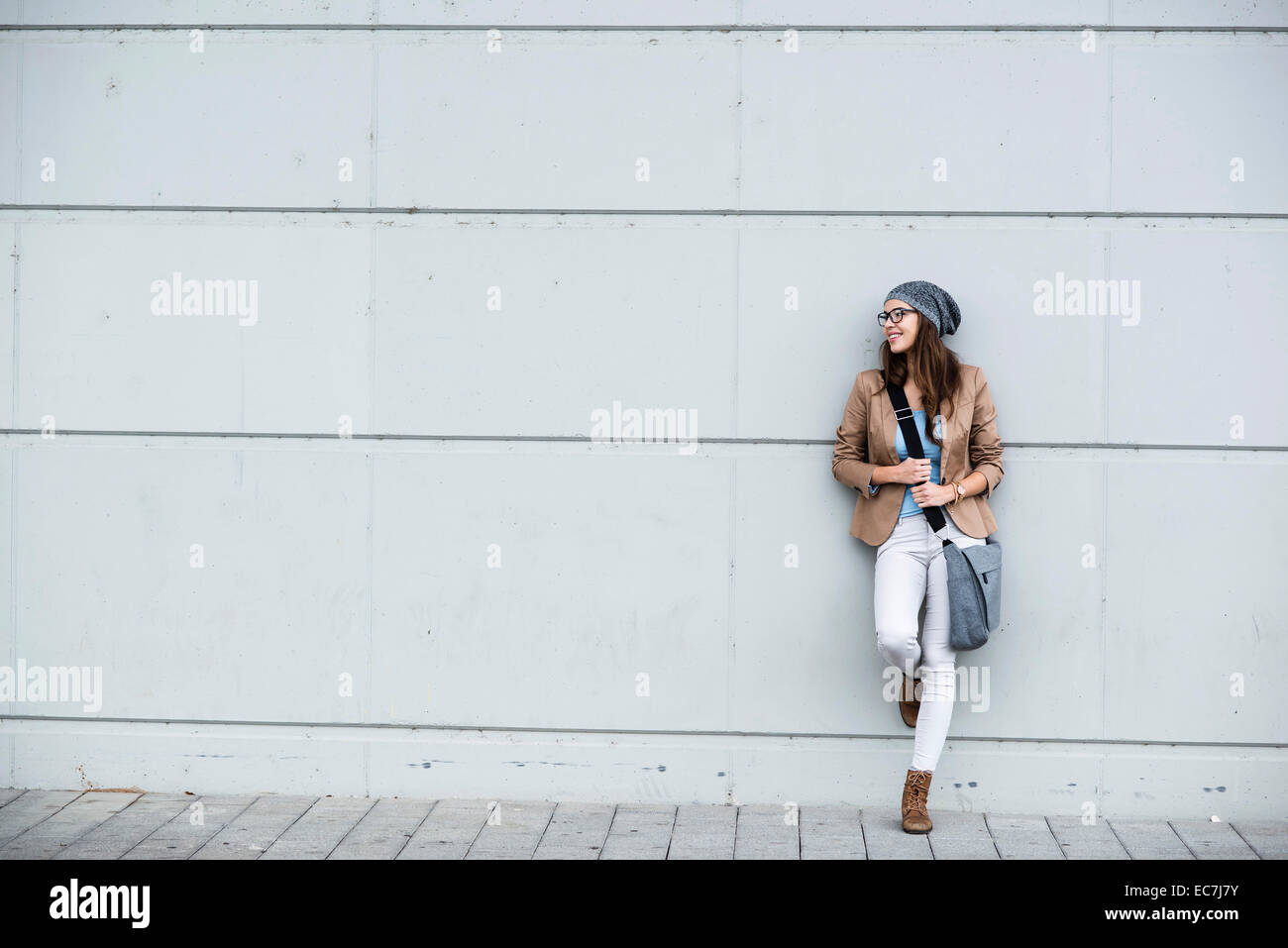 Young smiling woman leaning against a wall waiting Stock Photo - Alamy