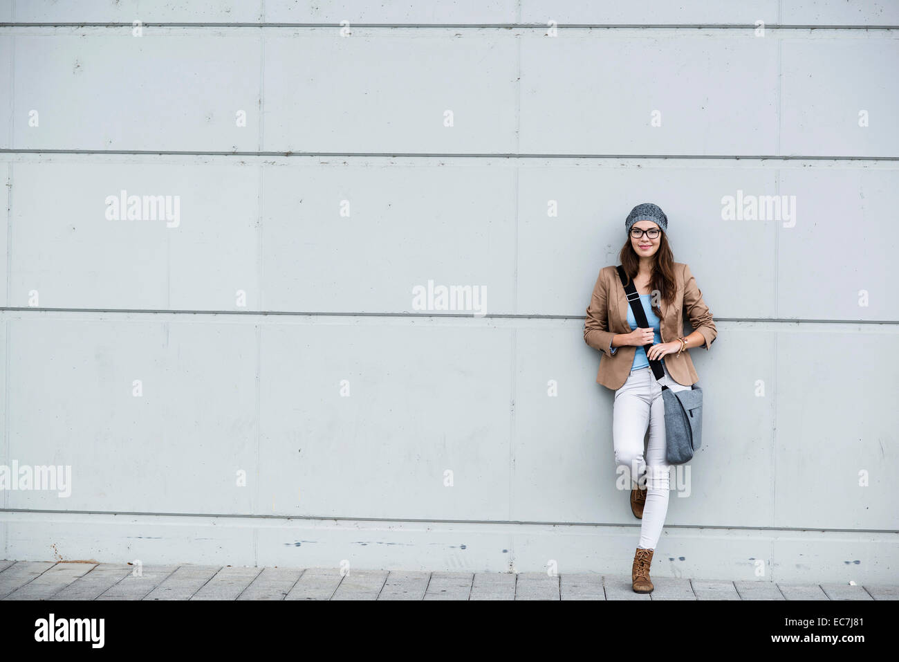 Young woman leaning against a wall waiting Stock Photo - Alamy