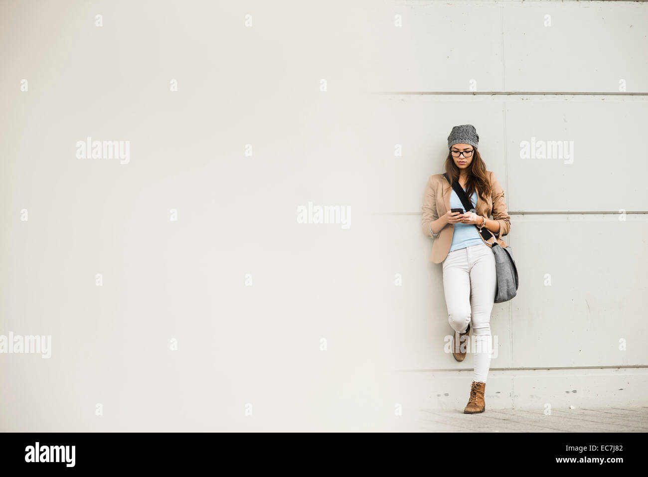 Young woman leaning against a wall waiting Stock Photo - Alamy