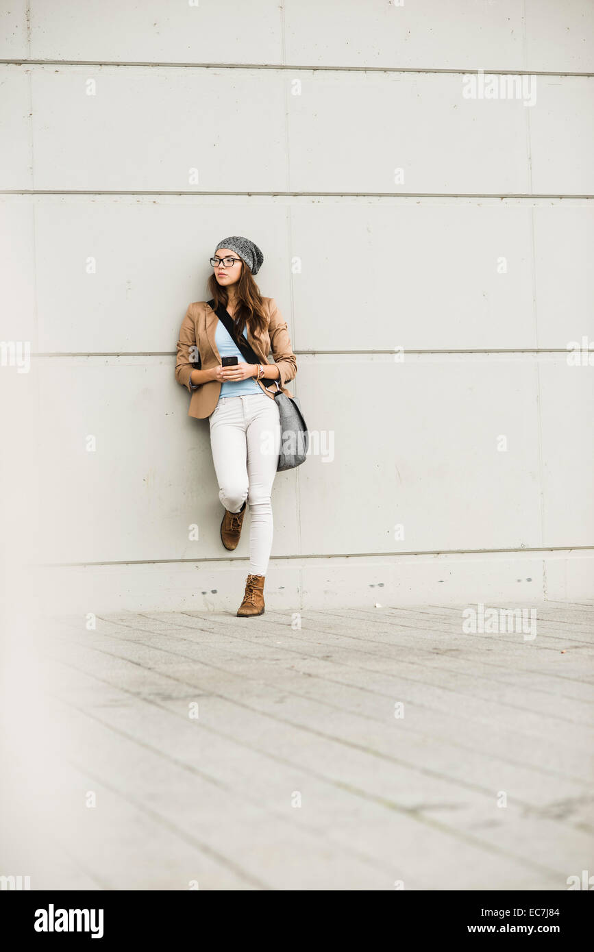Young woman leaning against a wall waiting Stock Photo - Alamy