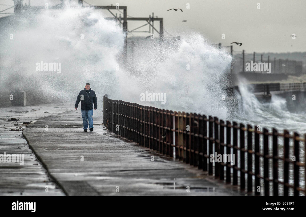 A man dodges the waves as they crash over the promenade wall on ...