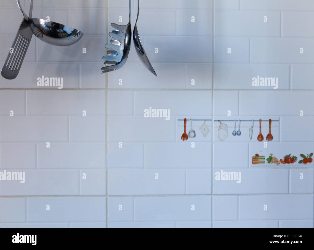 Cropped image of kitchen utensils hanging agains white metro tiles ...