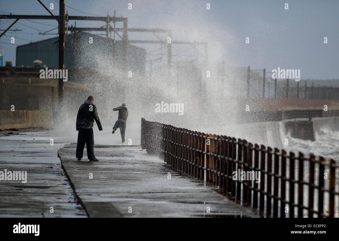 Men dodge the waves as they crash over the promenade wall on December ...