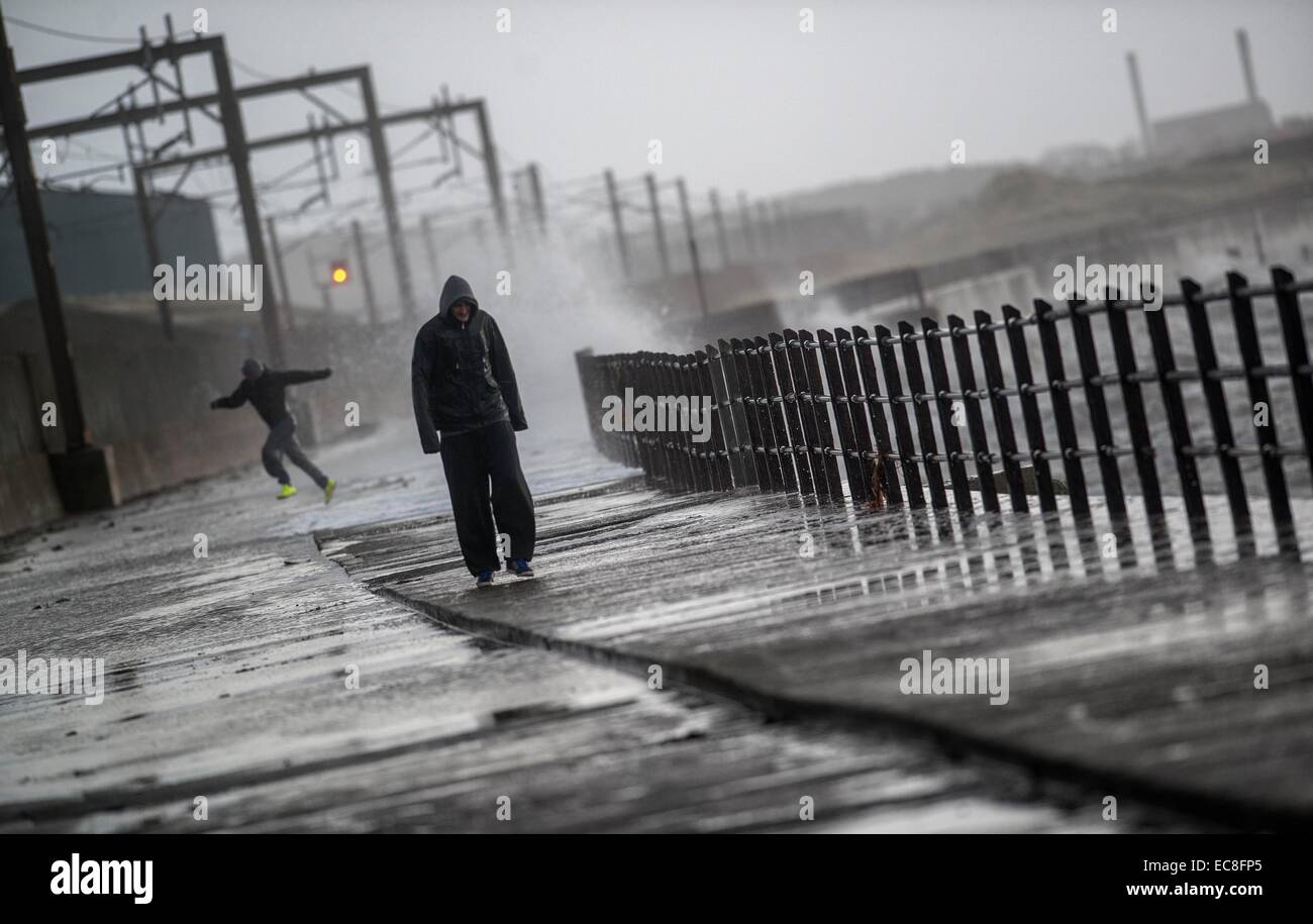 Men dodge the waves as they crash over the promenade wall on December ...