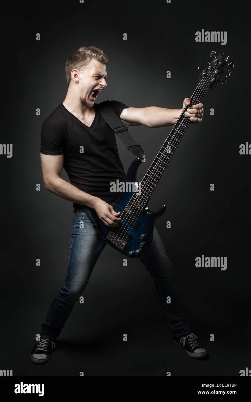 young male musician playing a six-string bass guitar isolated on dark ...